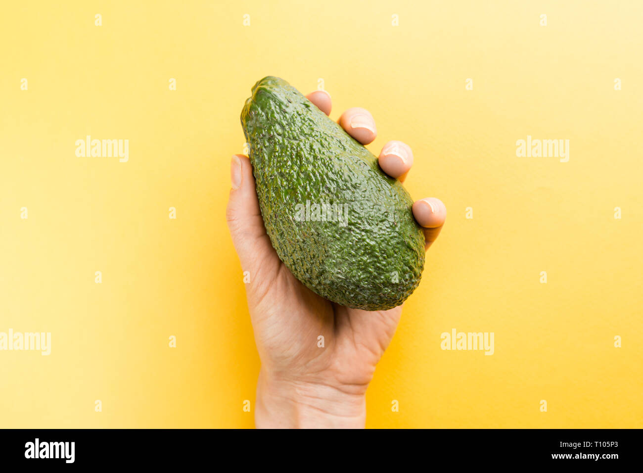 Organic green whole avocado fruit in a hand on yellow background. Top ...