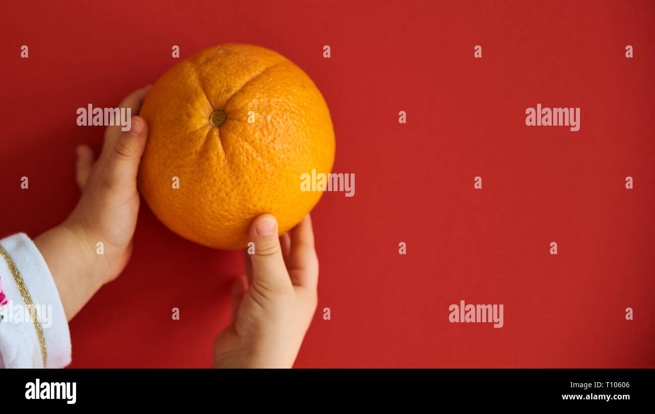 Baby grabbing an orange fruit with both hands. Red color background ...