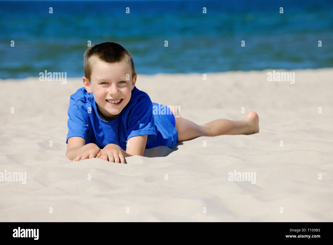 Smiling boy lying on a sandy beach Stock Photo - Alamy