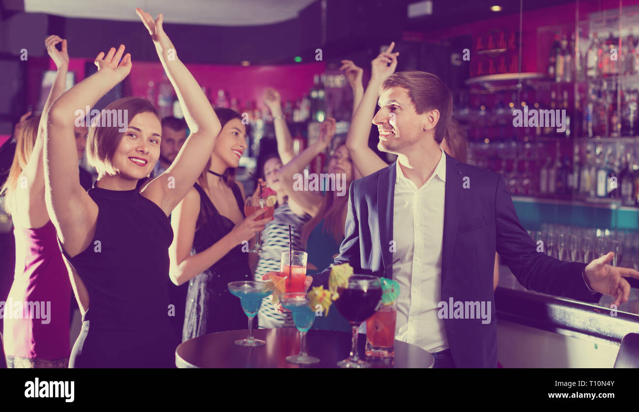 Cheerful glad colleagues dancing on corporate party with cocktails in ...