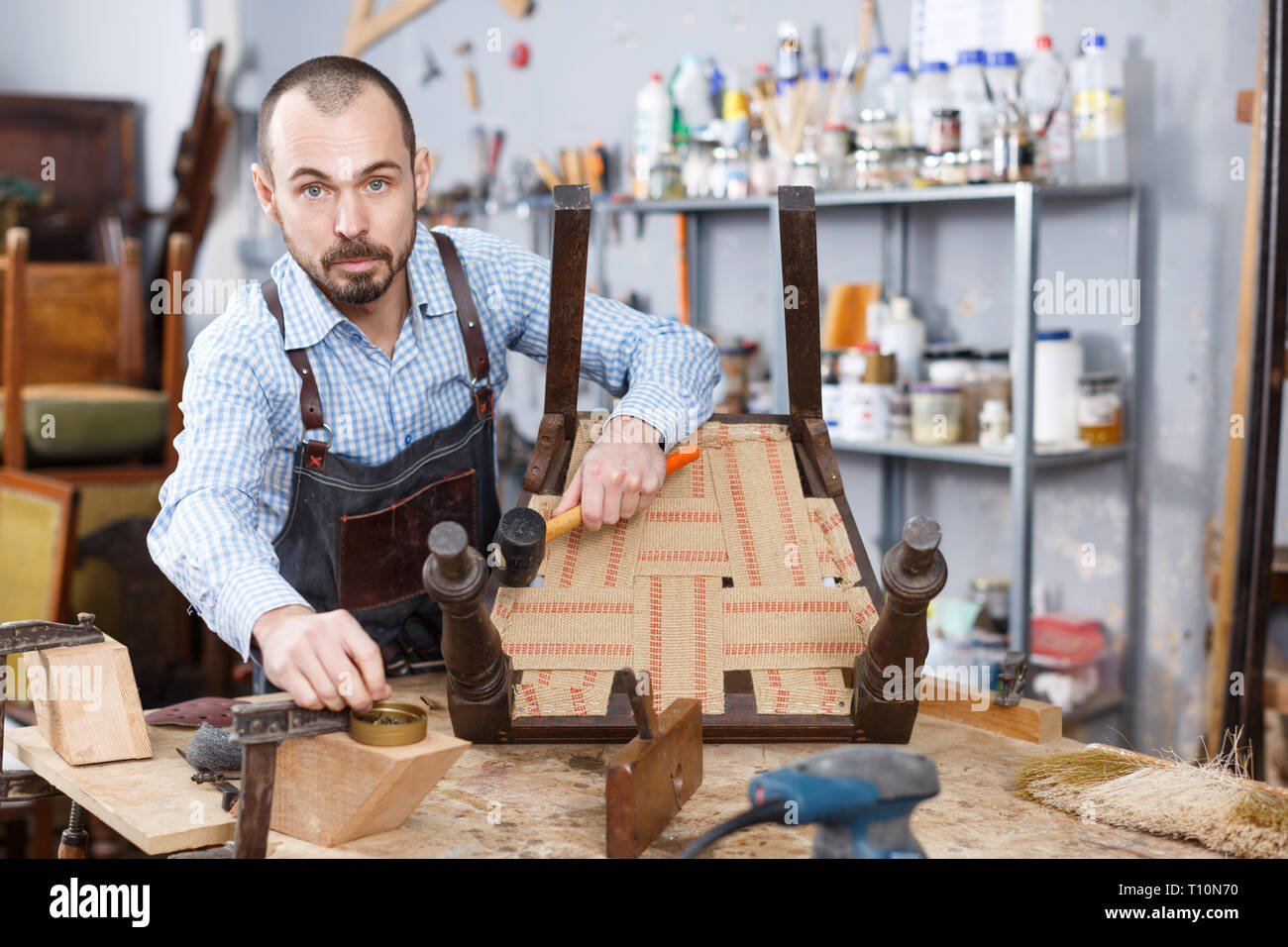 Skilled workman working at repair shop, restoring antique armchair ...