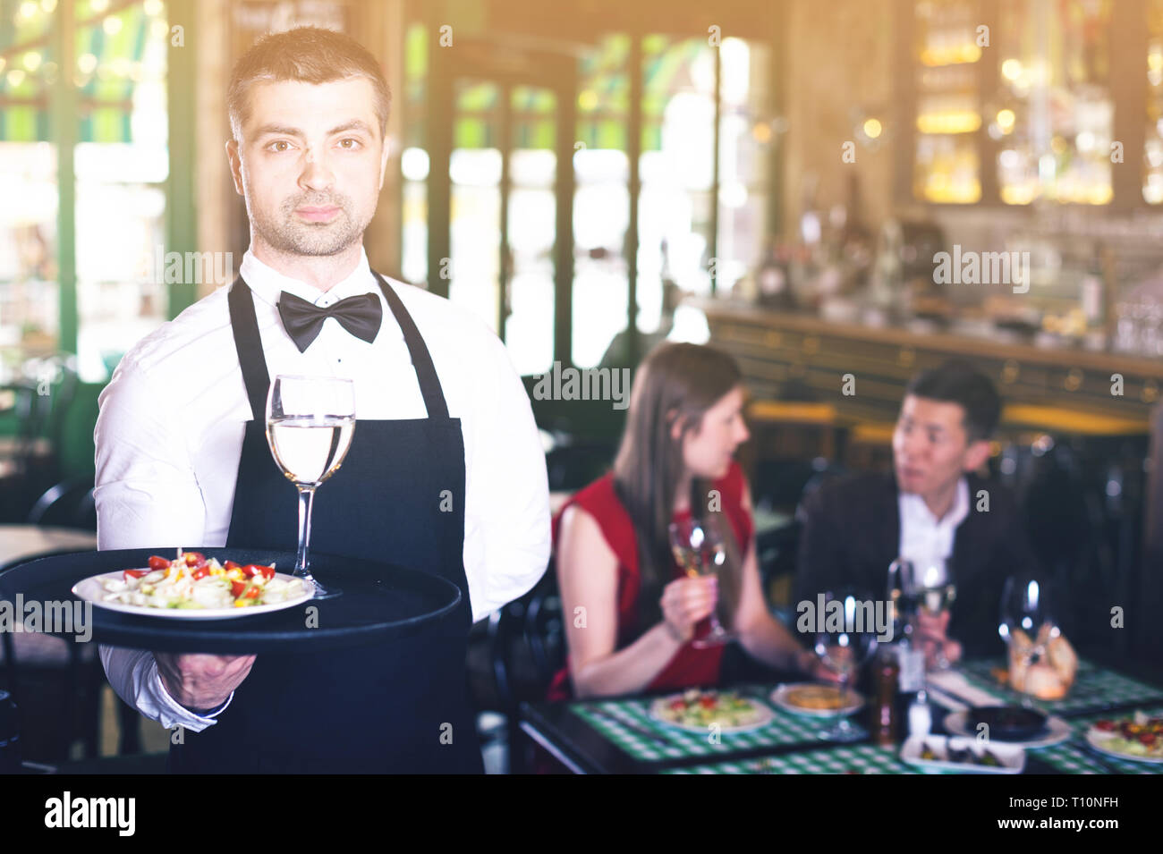 Man waiter is holding tray with wine and salad for clients in ...