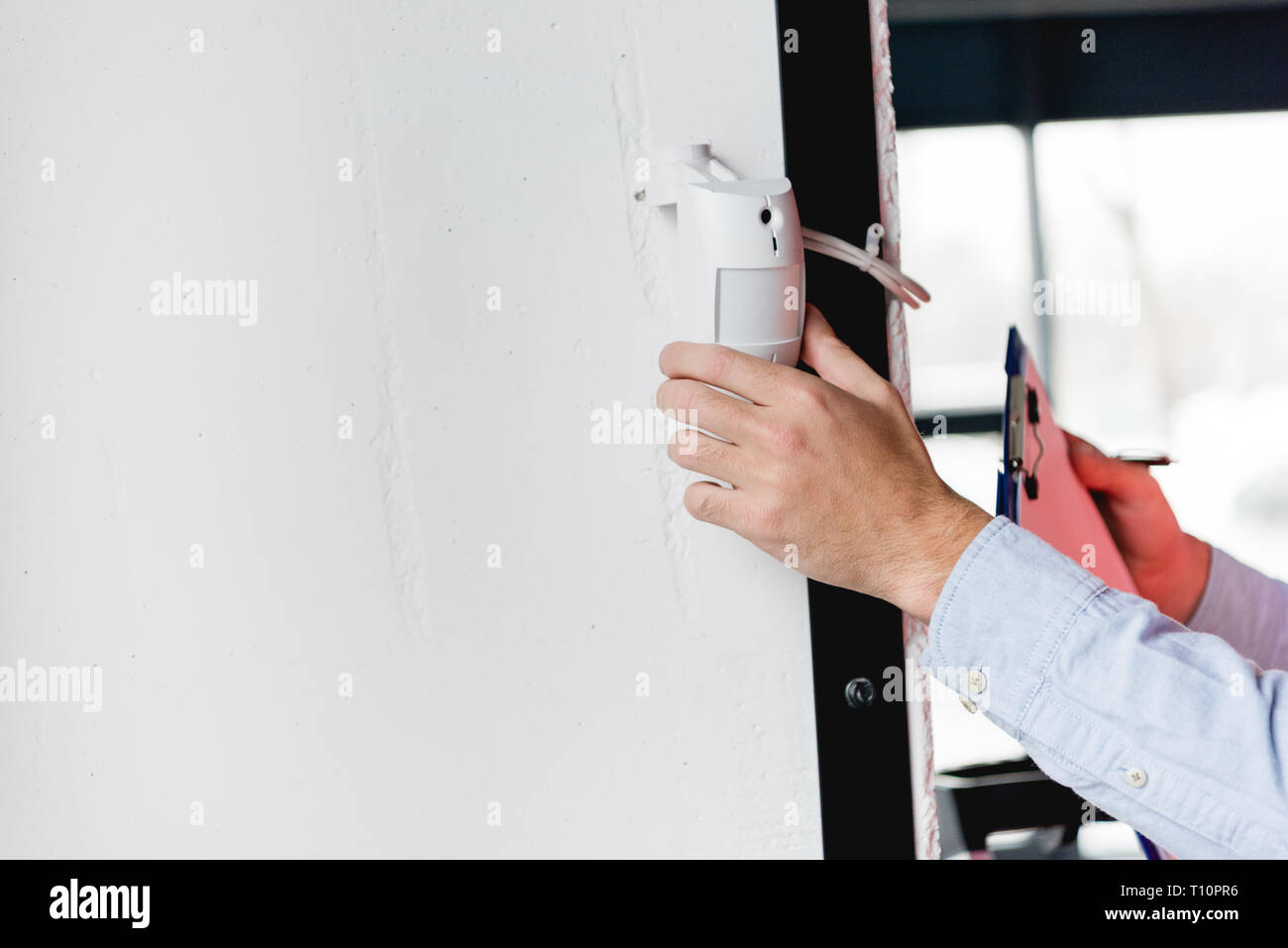cropped view of fireman checking fire alarm while holding clipboard and ...