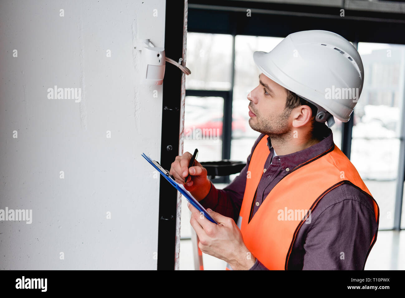 confident fireman in helmet looking at fire alarm while holding ...