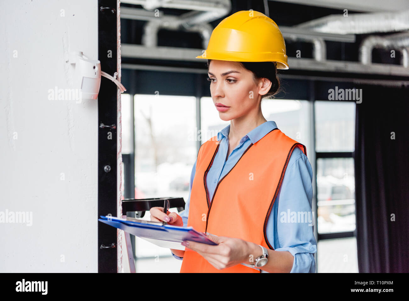 serious female firefighter standing near fire alarm while holding ...