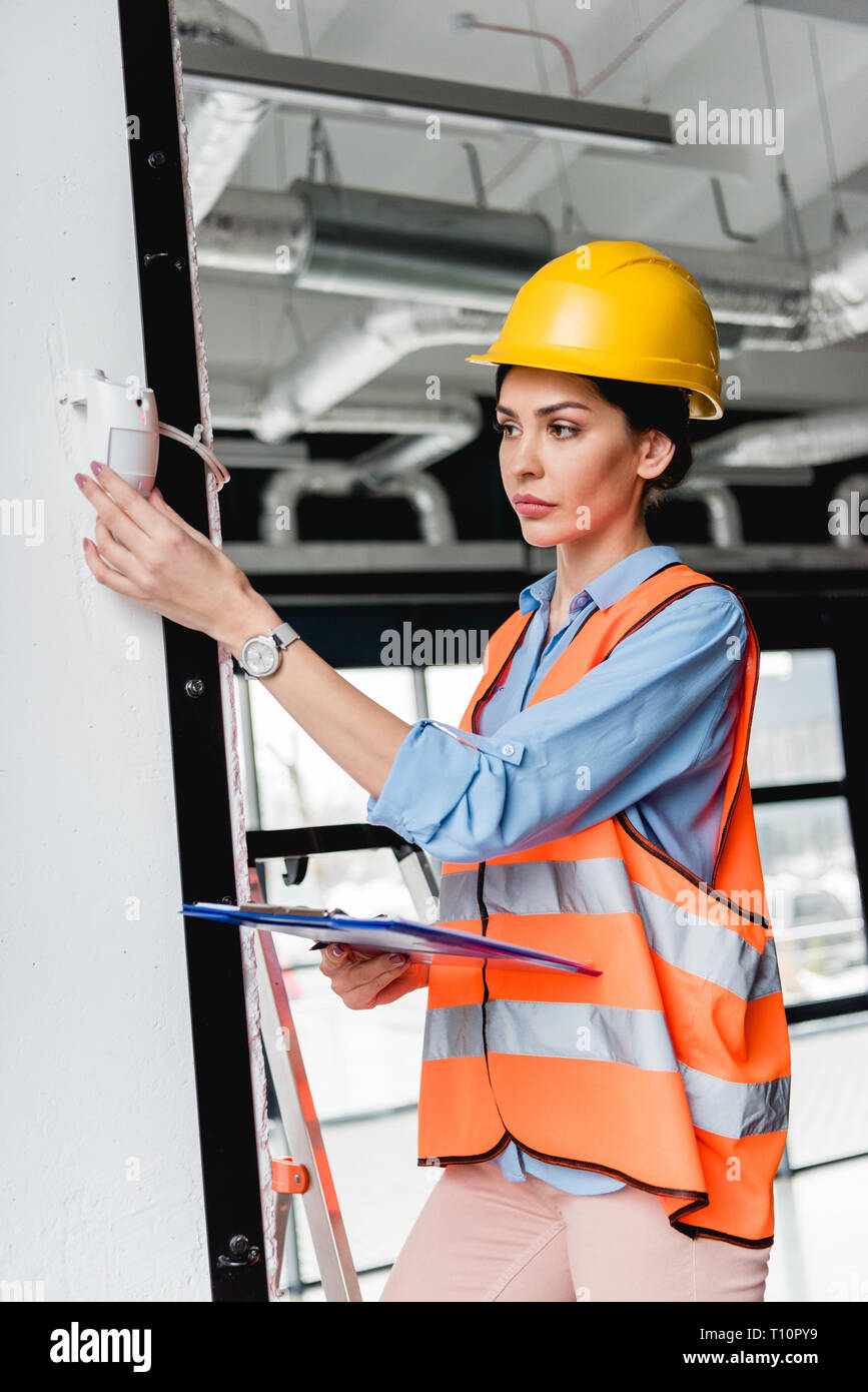 attractive firefighter checking fire alarm while holding clipboard ...