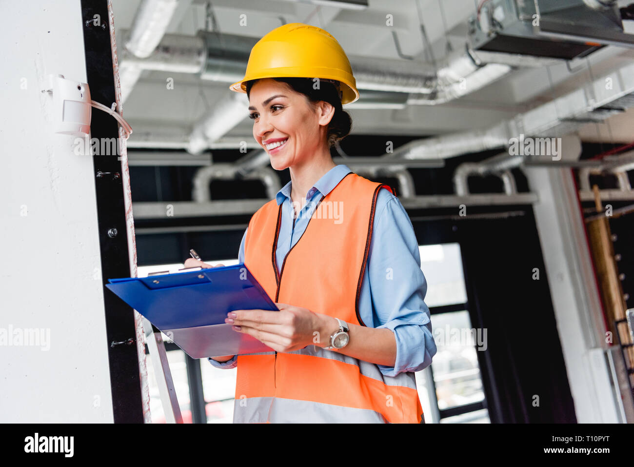 cheerful female firefighter standing near fire alarm while holding ...