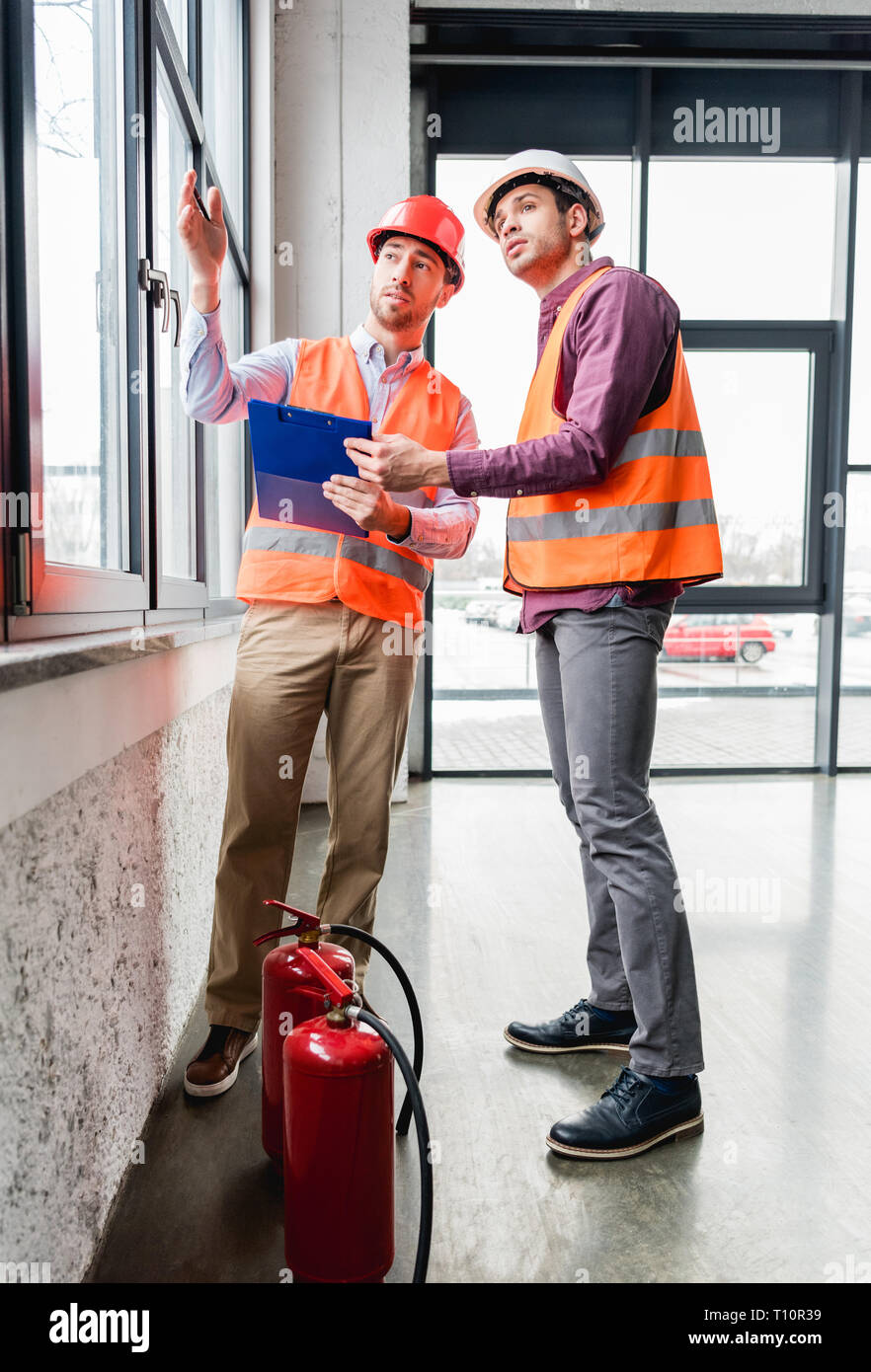 firemen in helmets talking while standing near red extinguishers Stock ...