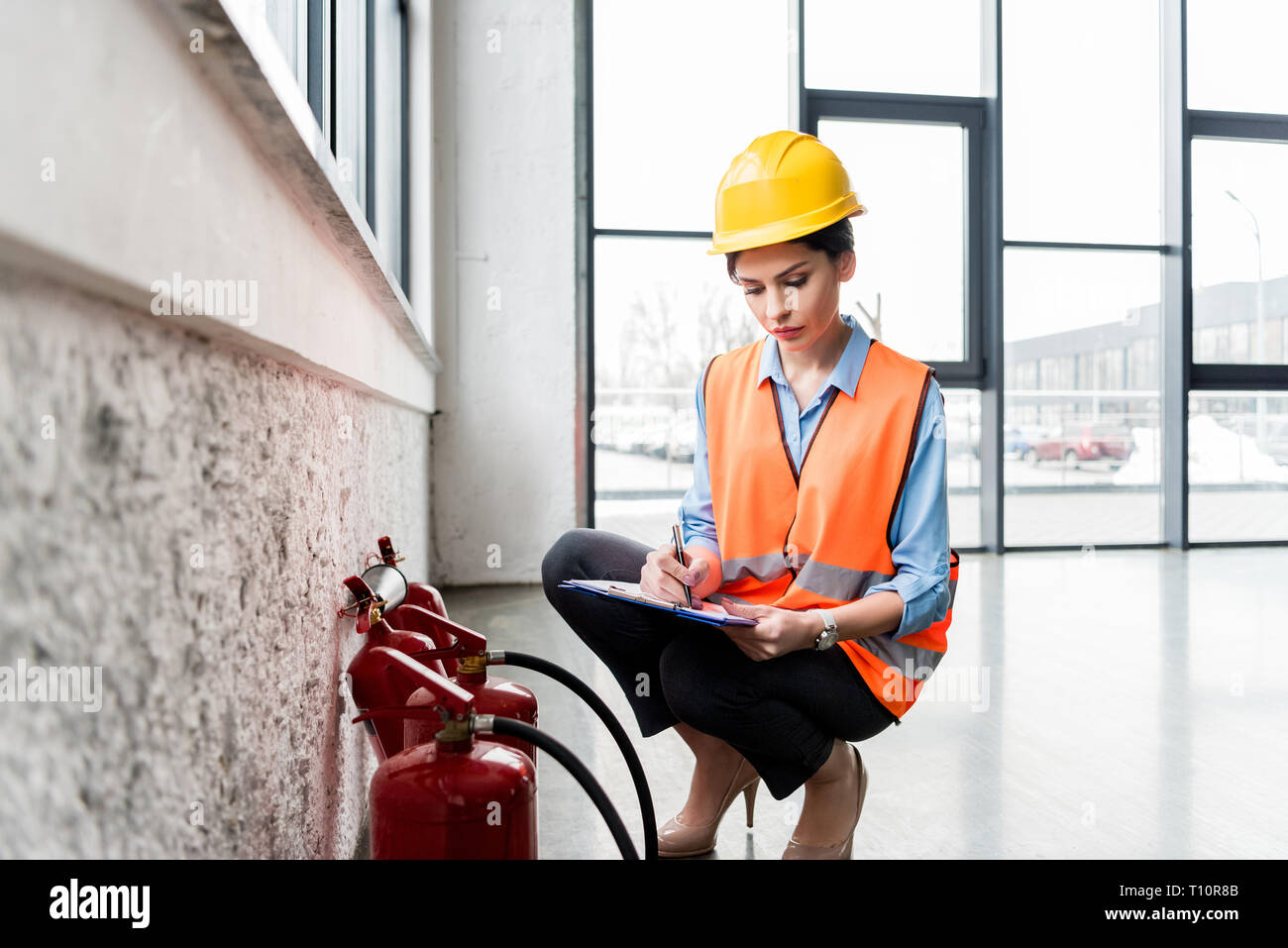 beautiful firefighter in helmet writing on clipboard while checking ...
