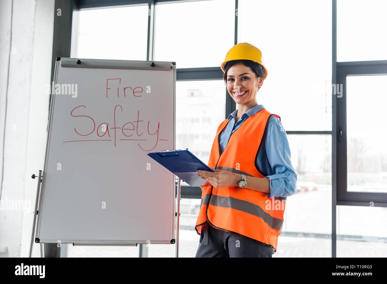 happy female firefighter in helmet holding clipboard and pen while ...
