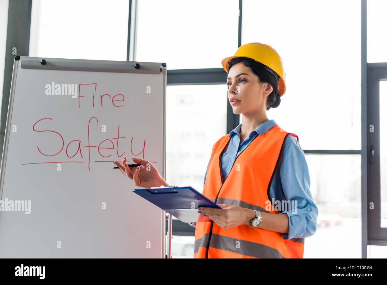 female firefighter in helmet holding clipboard and pen while standing ...
