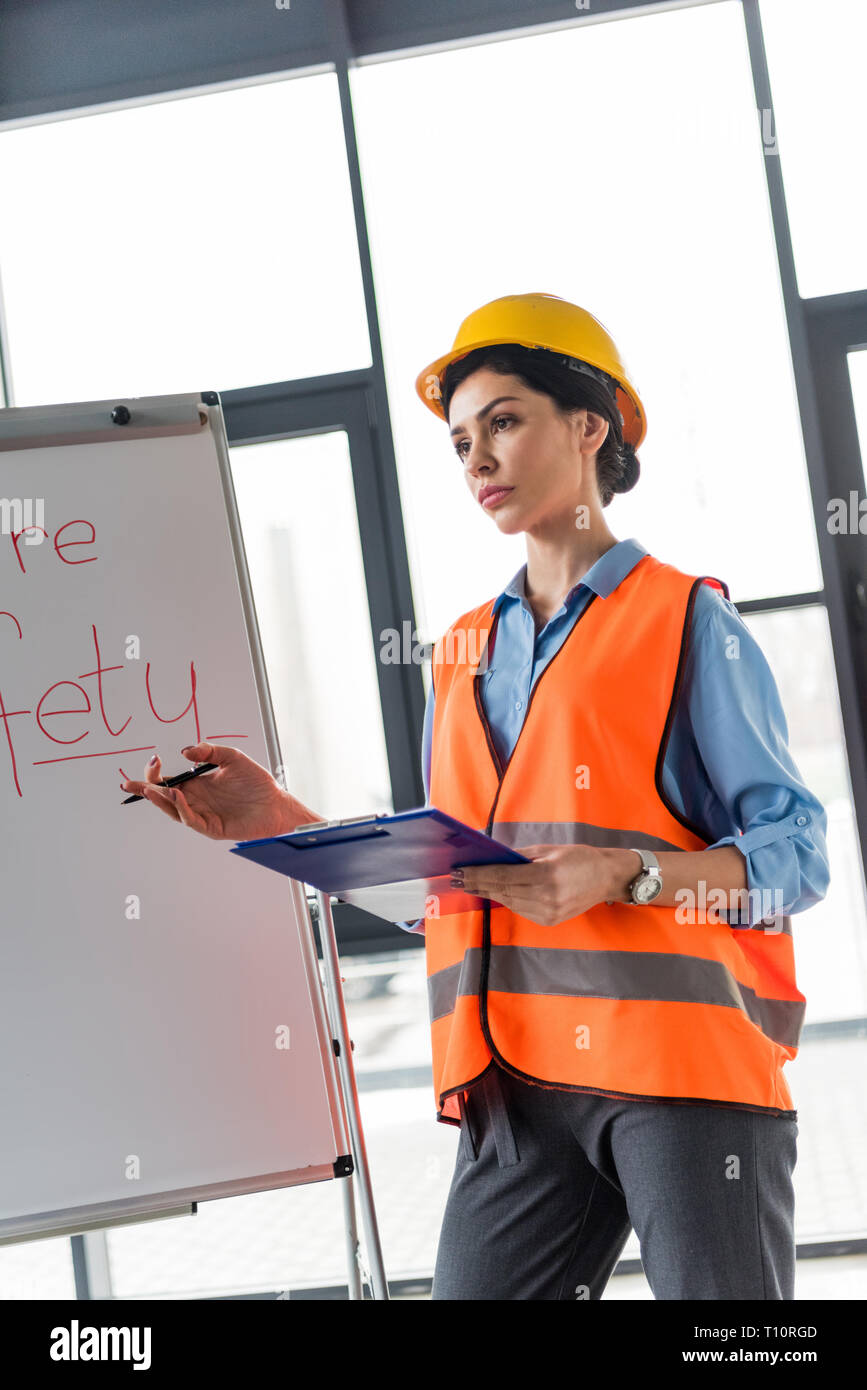 serious female firefighter in helmet holding clipboard and pen while ...