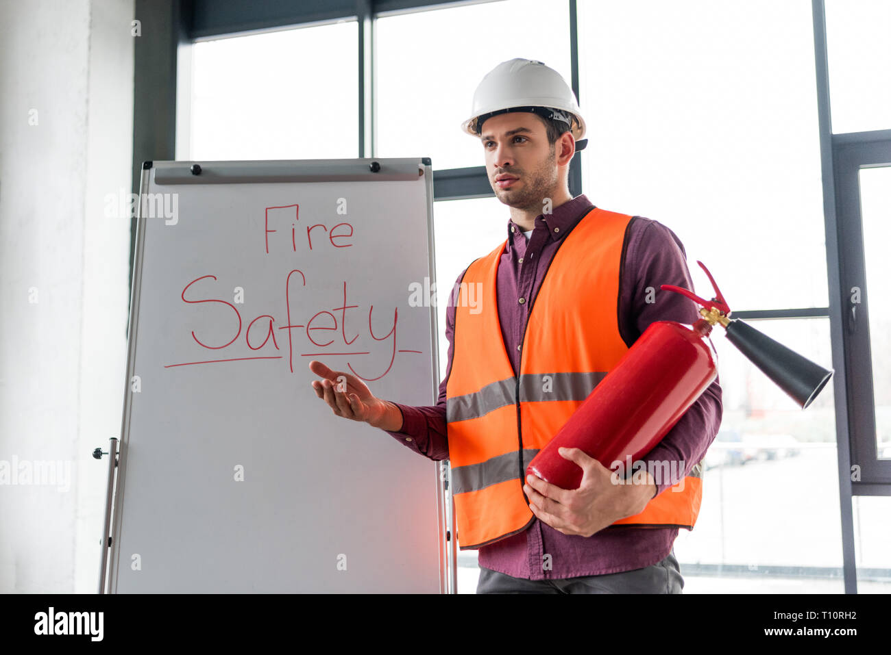 handsome fireman holding red extinguisher while standing near white ...