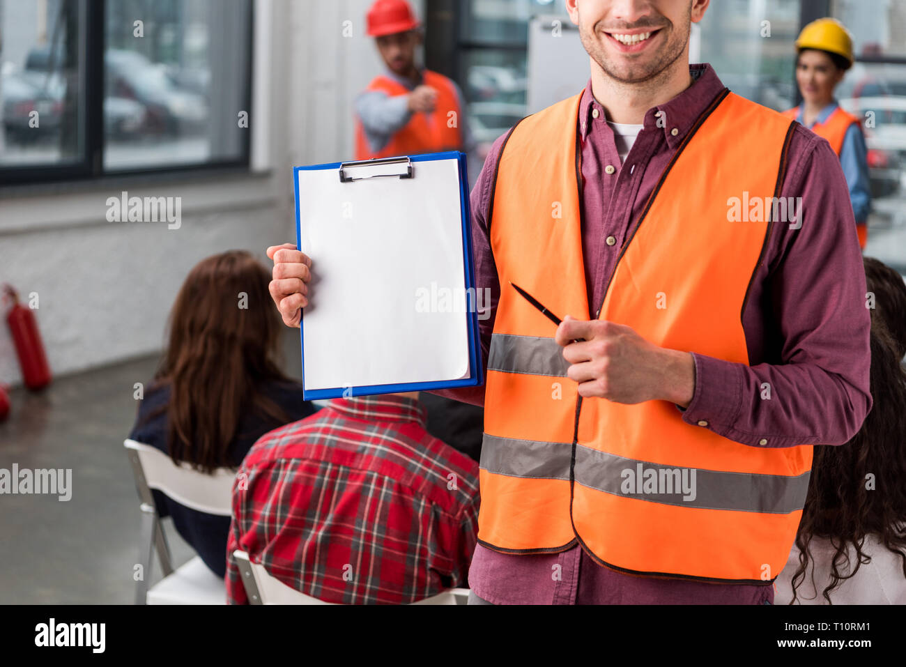 cropped view of cheerful fireman pointing at blank clipboard with pen ...