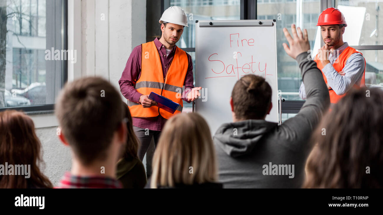 selective focus of handsome firemen in helmets giving talk on briefing ...