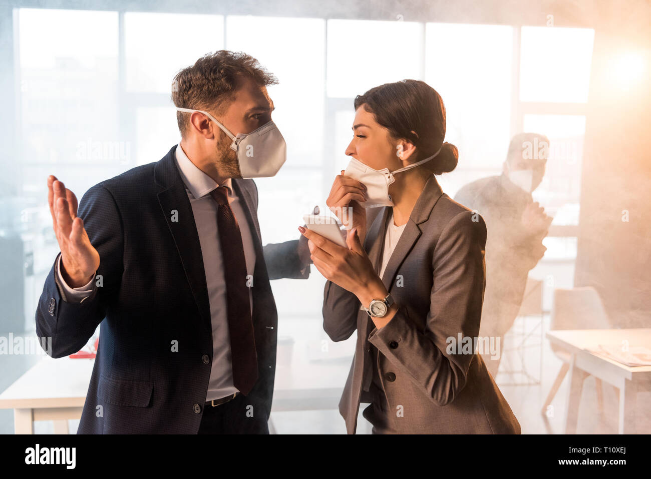 selective focus of terrified woman in mask looking at scared coworker ...