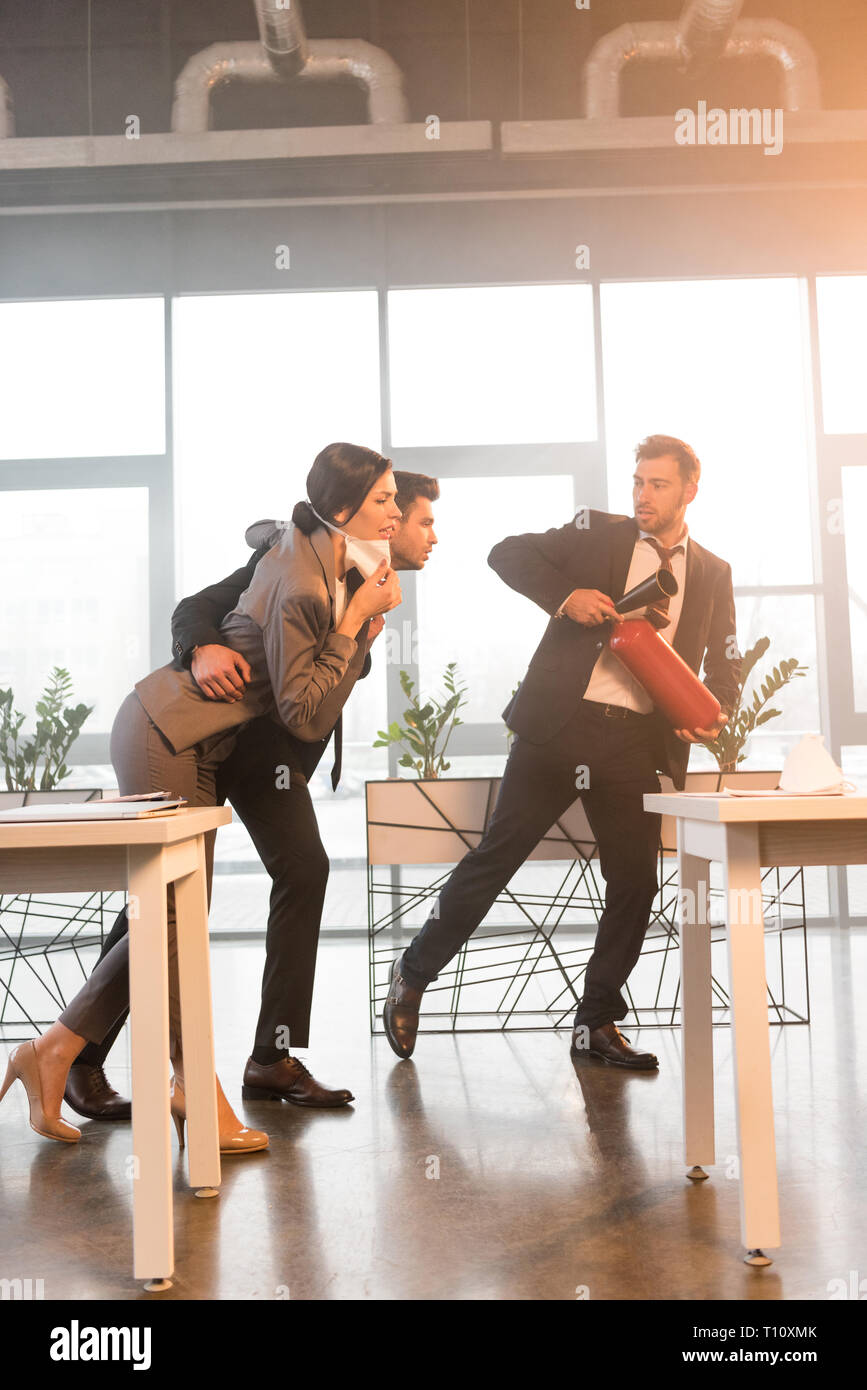 scared businessman holding extinguisher near colleagues while walking ...