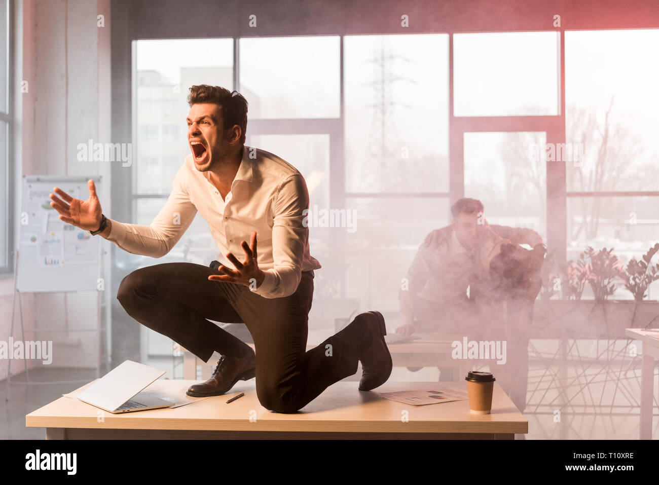 terrified businessman screaming while sitting on desk with laptop near ...
