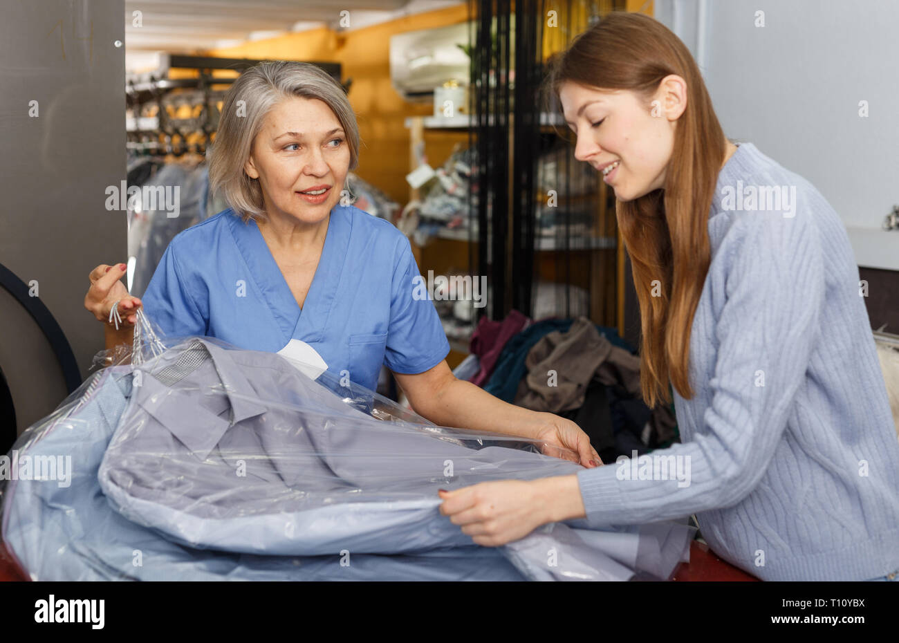 Female worker of dry-cleaning salon giving woman her clean clothes in ...