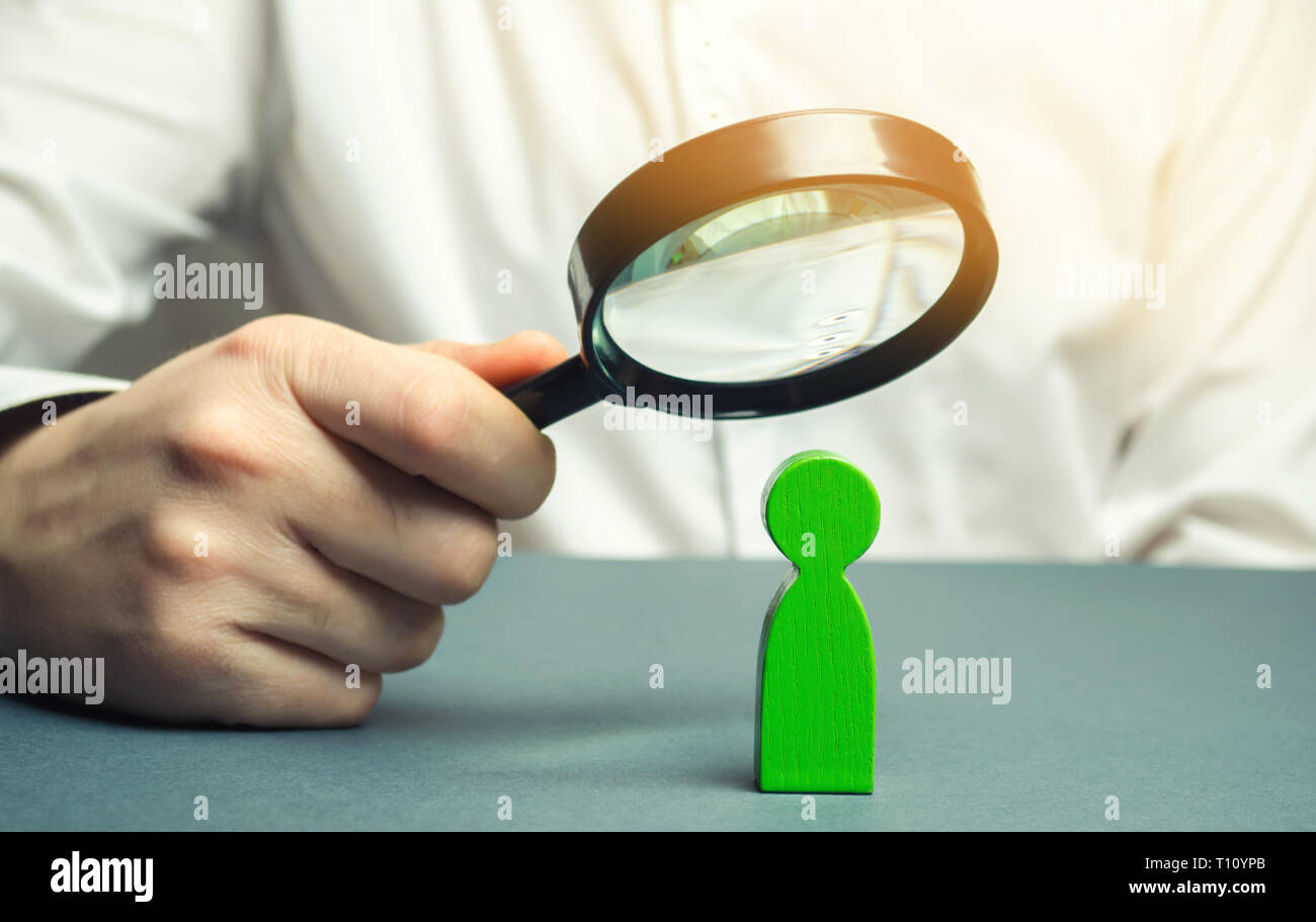 A businessman is holding a magnifying glass over a green man figure ...