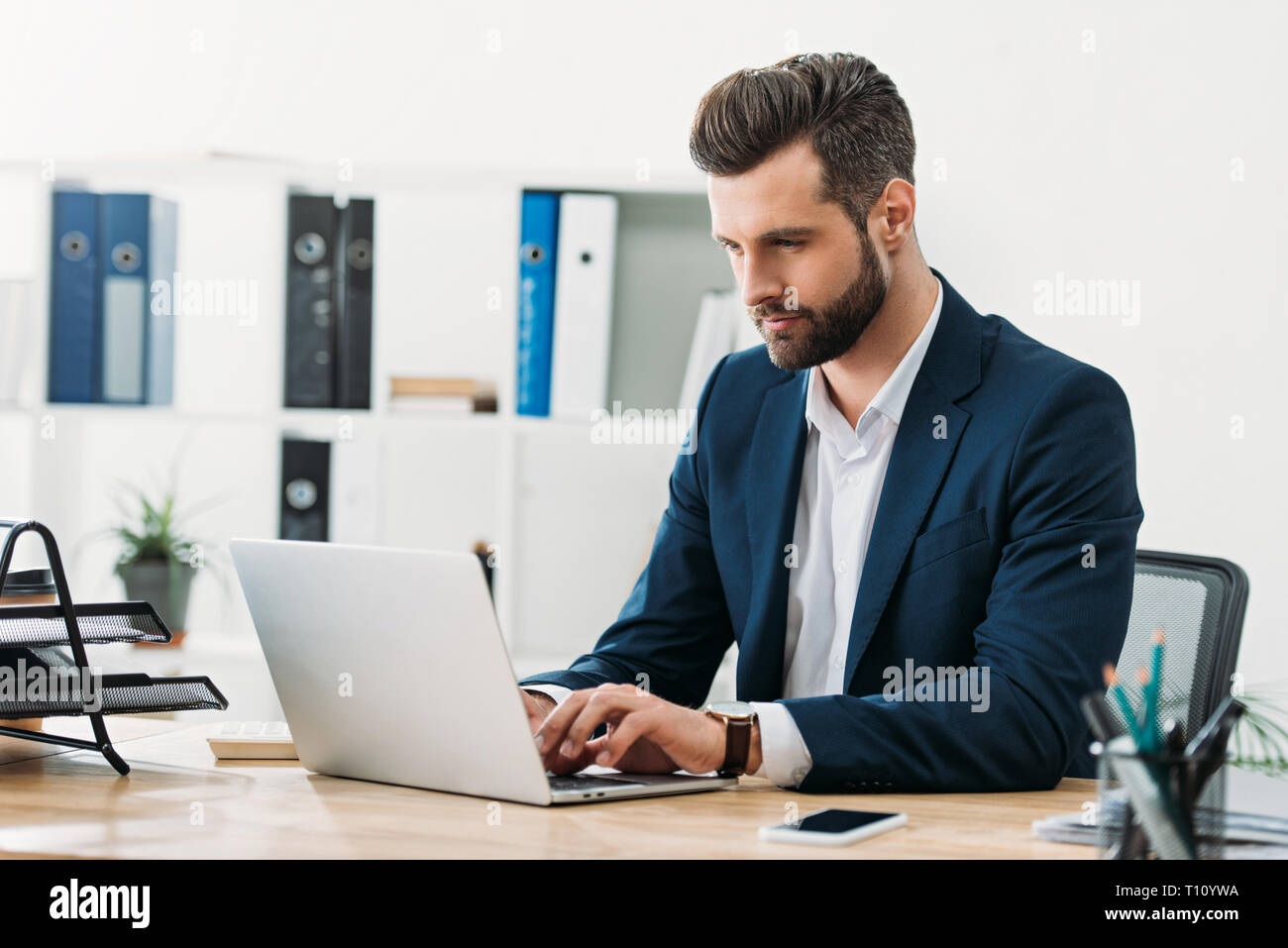 businessman in blue suit sitting at table with laptop and typing in ...
