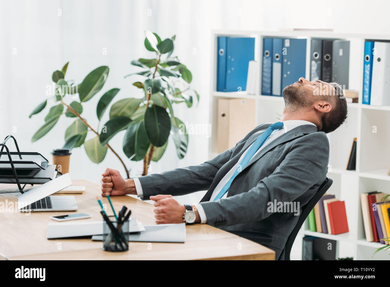 businessman sitting at table with laptop and leaned back in chair in ...