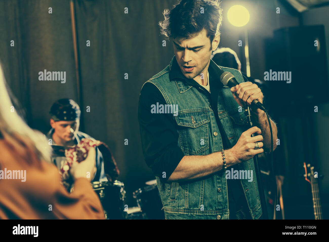 selective focus of handsome singer standing with microphone near rock ...
