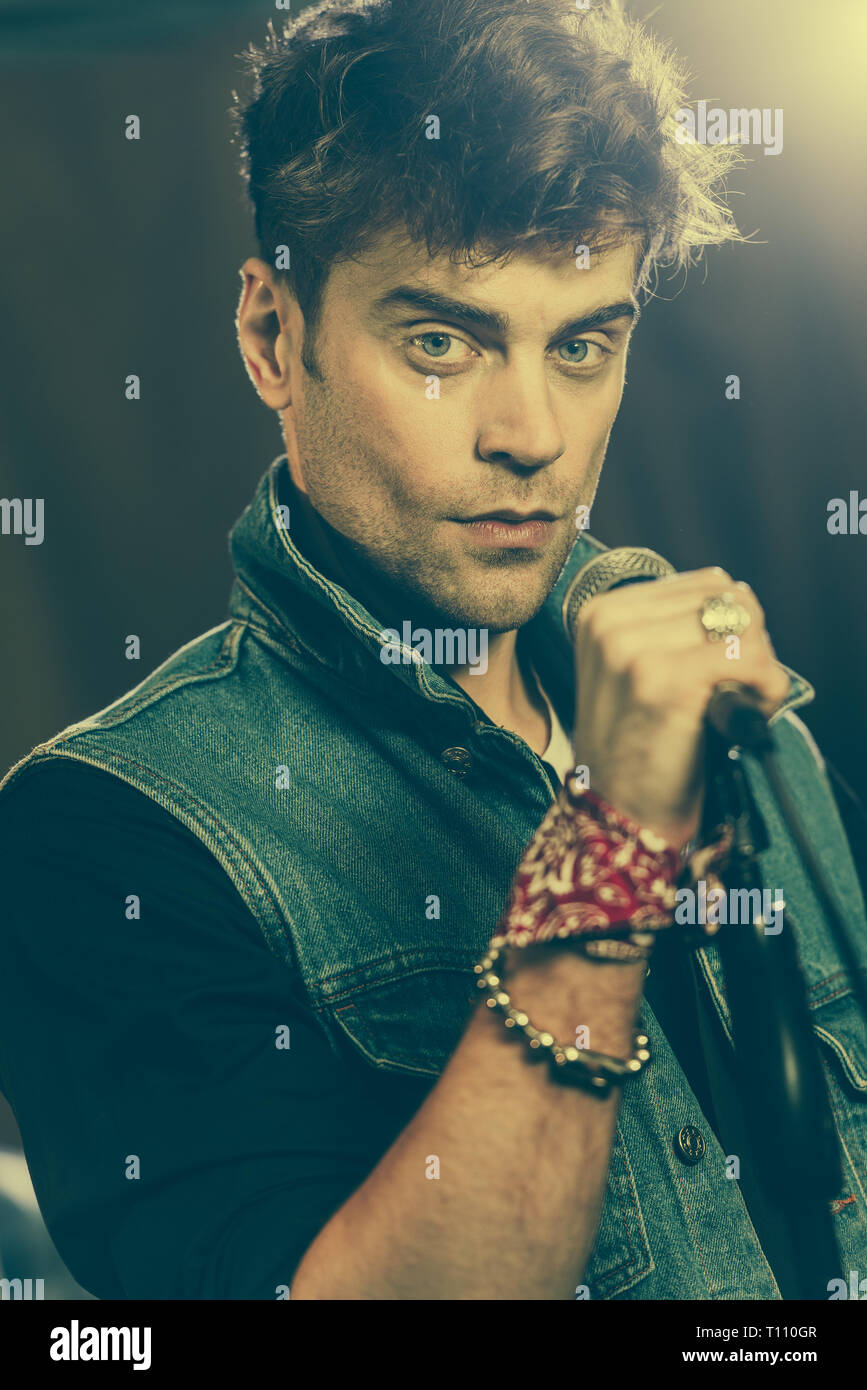 handsome trendy singer standing near microphone and looking at camera ...