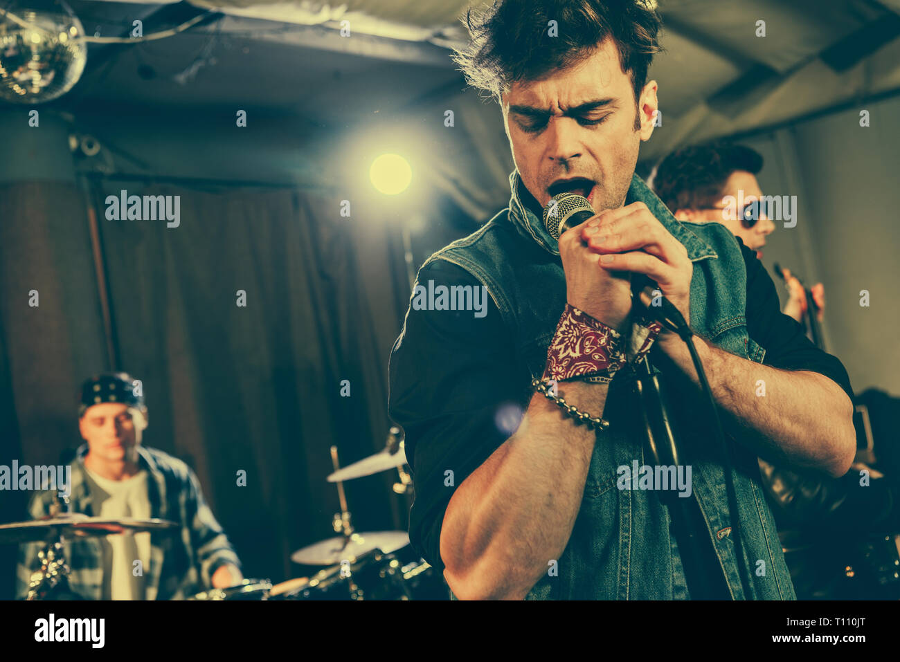 selective focus of man singing song with rock band performing on stage ...
