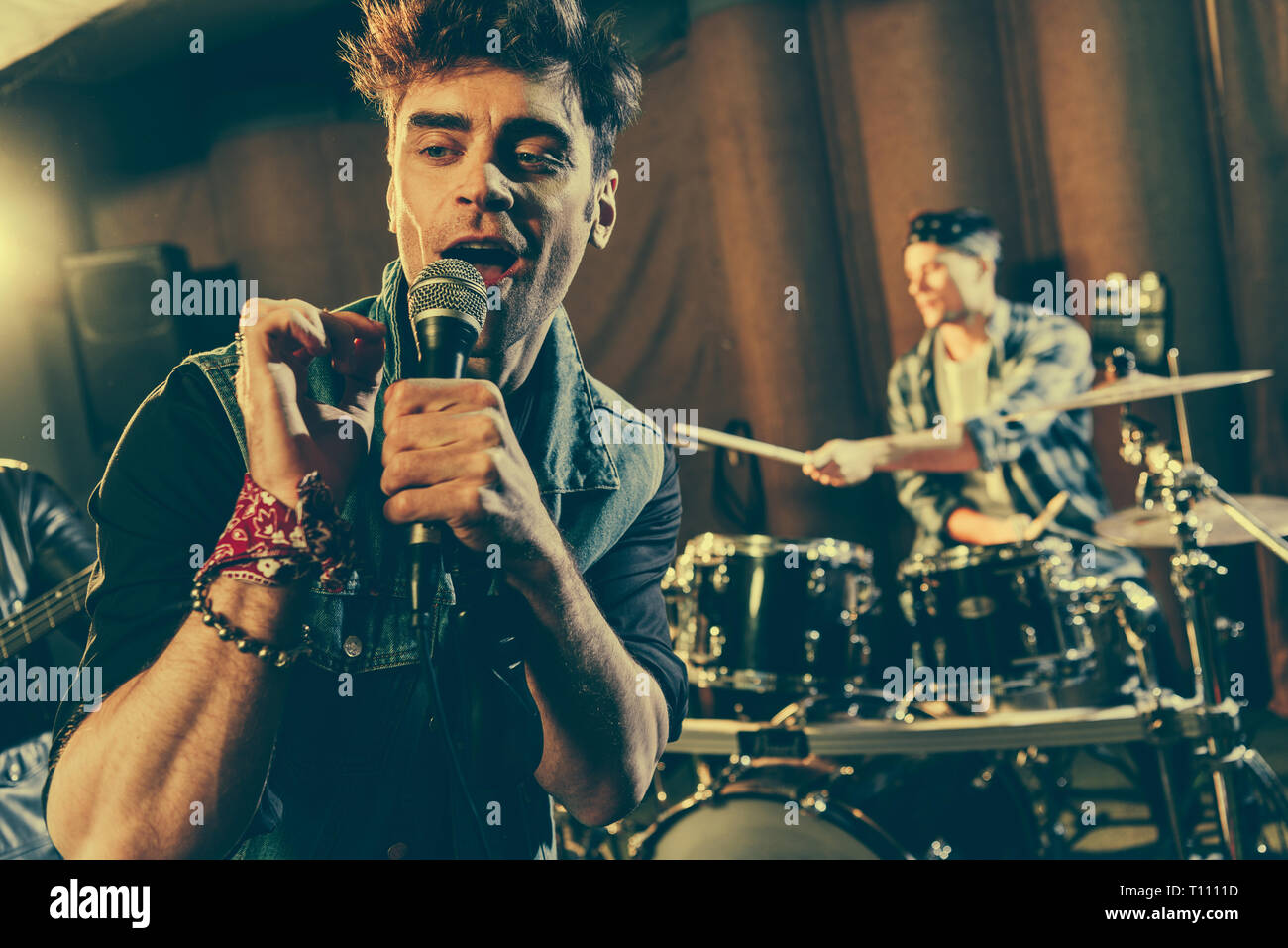 selective focus of good-looking singer singing in microphone near rock ...