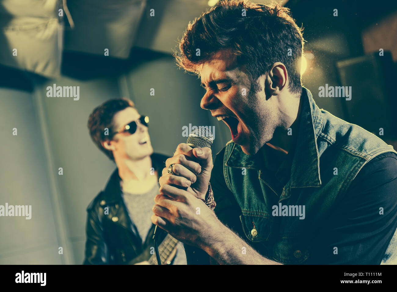 selective focus of stylish singer singing in microphone near rock band ...