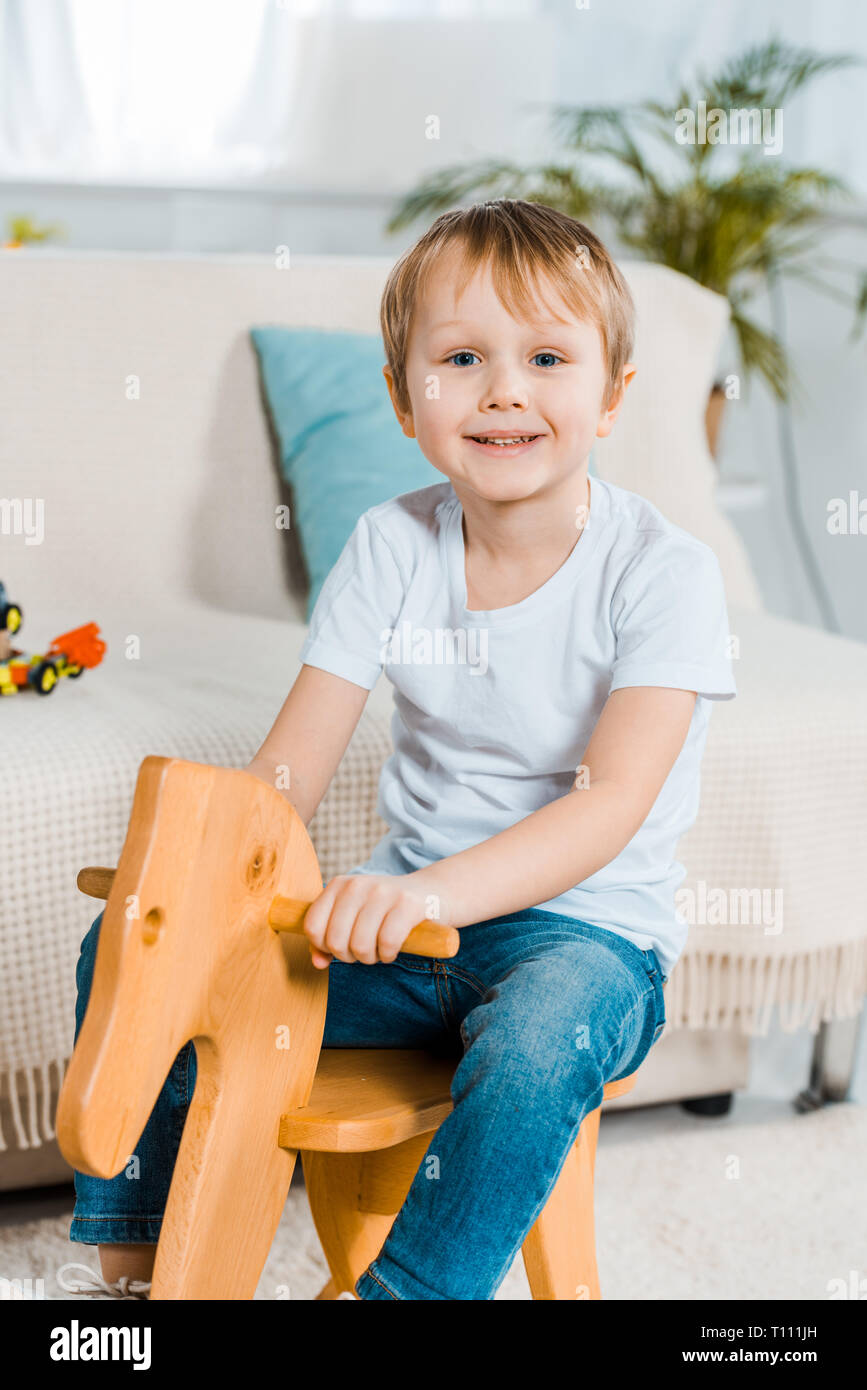 adorable smiling preschooler boy riding rocking horse at home and ...