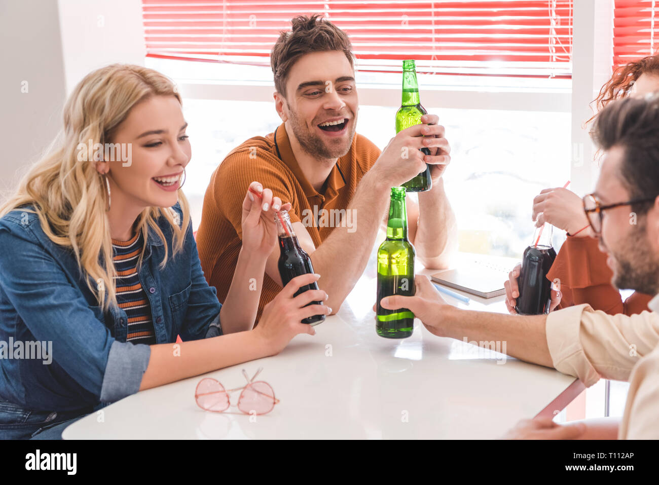 smiling friends holding glass bottles with soda and beer and talking at ...