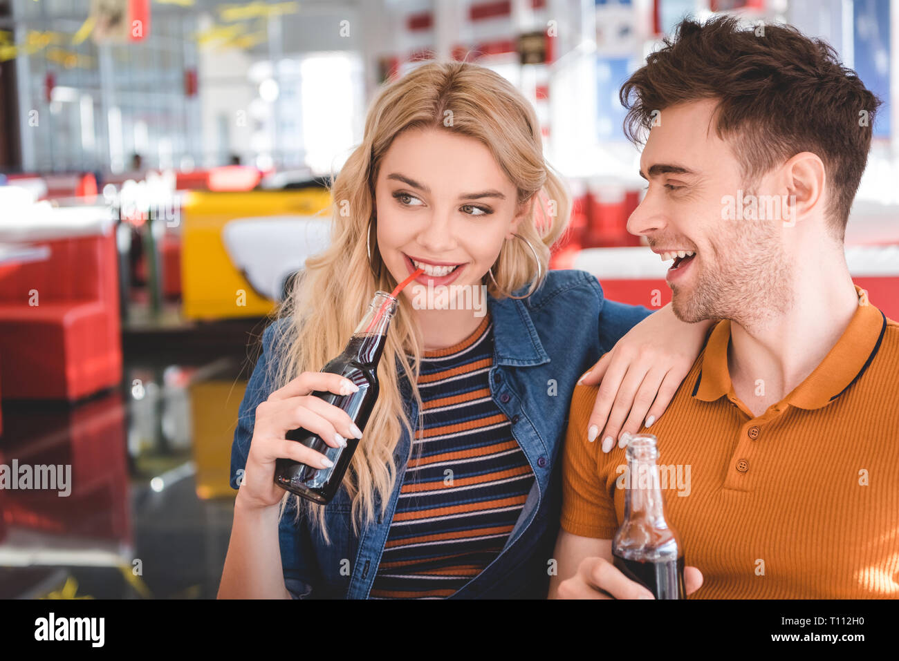 beautiful couple smiling, hugging and holding glass bottles at cafe ...