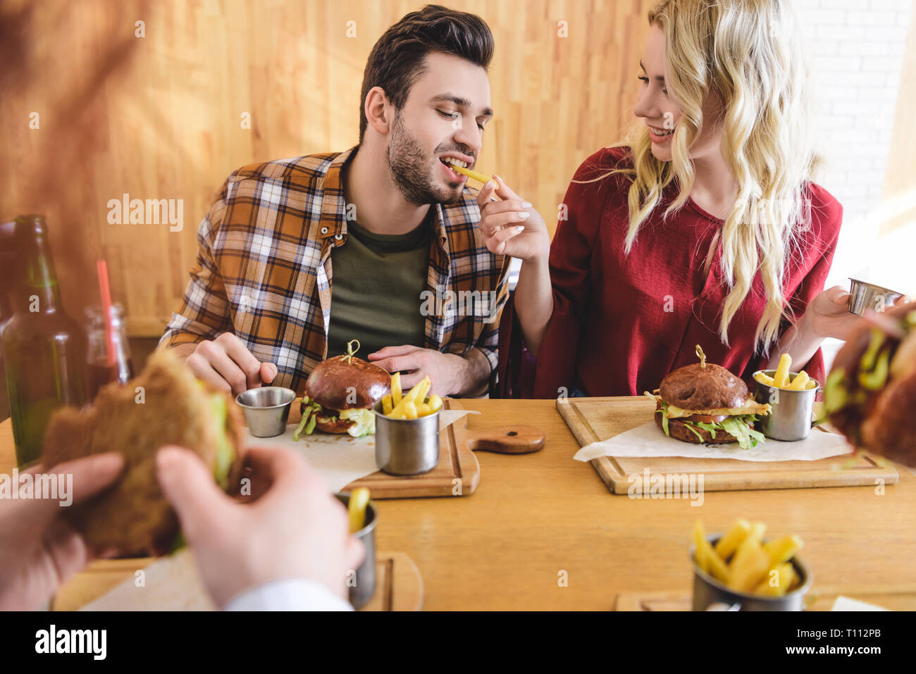 selective focus of handsome and beautiful friends eating burgers and ...