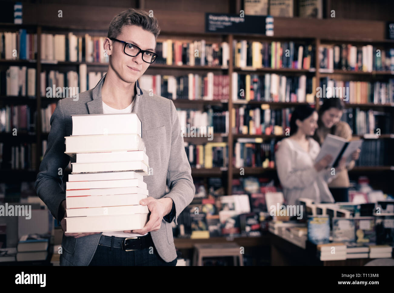 Portrait of young guy with stack of books in hands in bookshop Stock ...