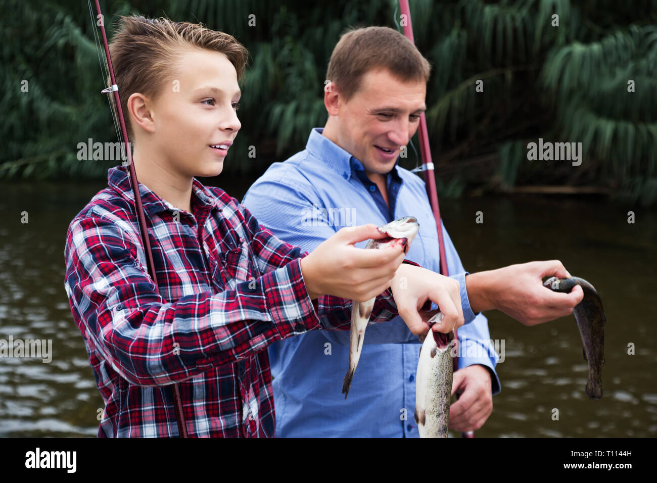 Smiling teenage boy and his father holding taken freshwater fish in ...