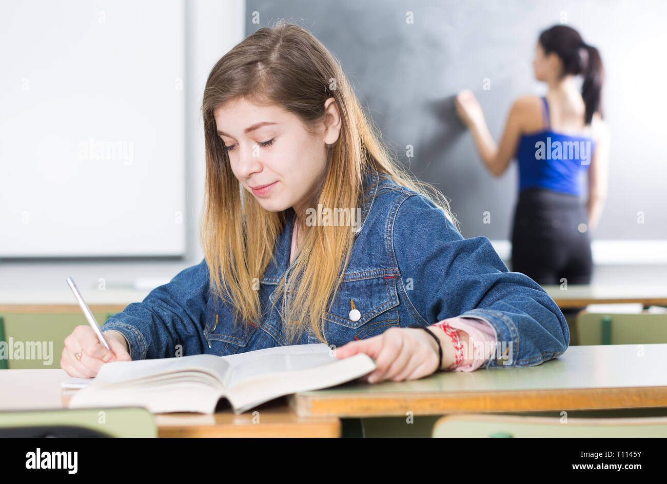 Girl is sitting at the desk and writing homework in the classroom Stock ...