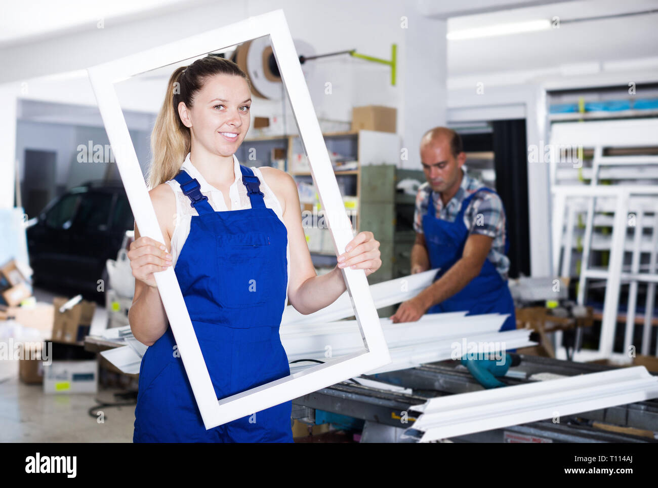Portrait of young smiling workwoman with plastic window frame in ...