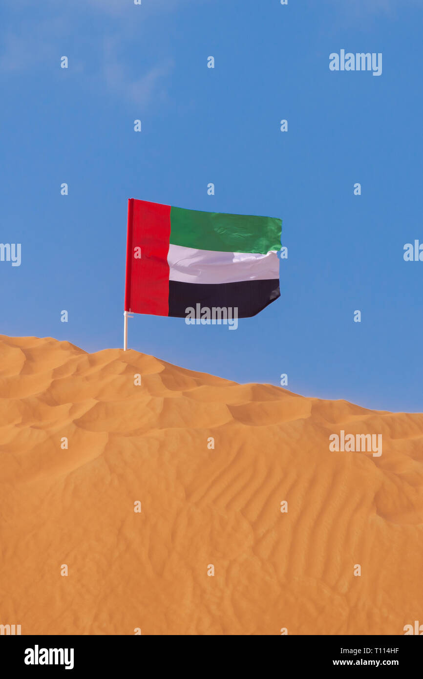 UAE Flag blowing in the wind on the top of an orange sand dune in the ...
