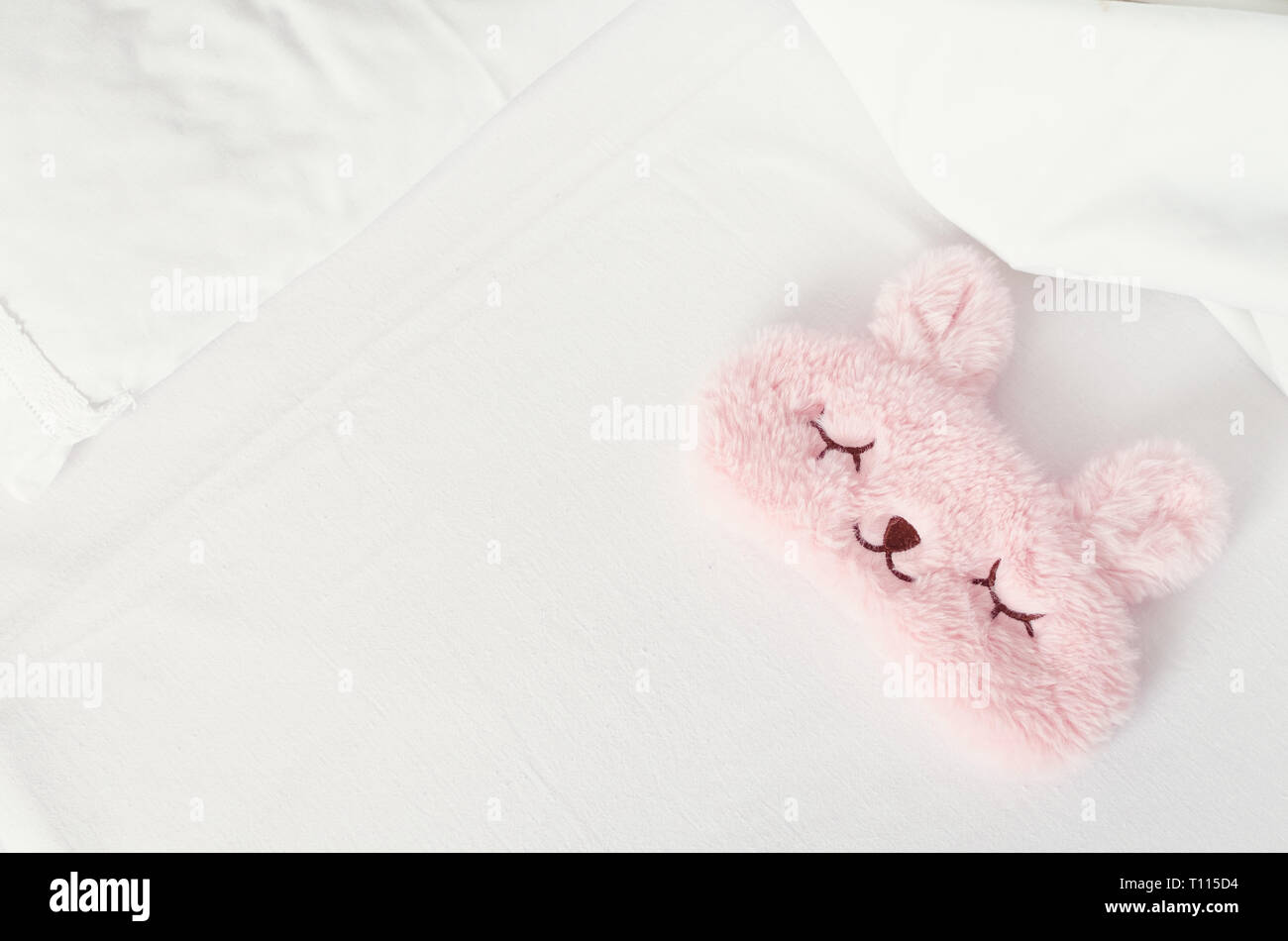 White bedding sheet, blanket and pillows with cute pink sleep mask on ...