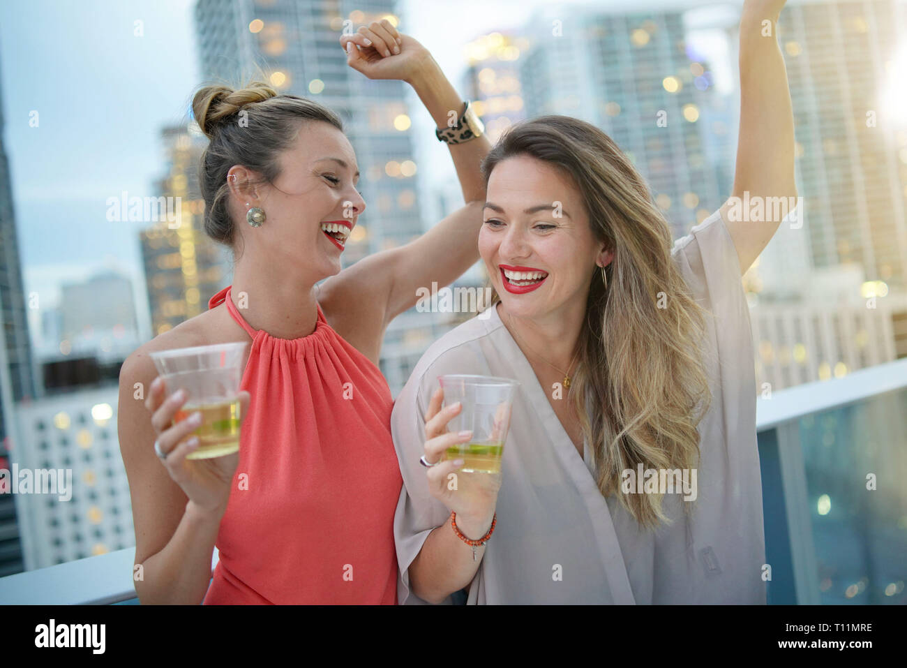 Two gorgeous friends having fun on rooftop bar in city at night fall ...