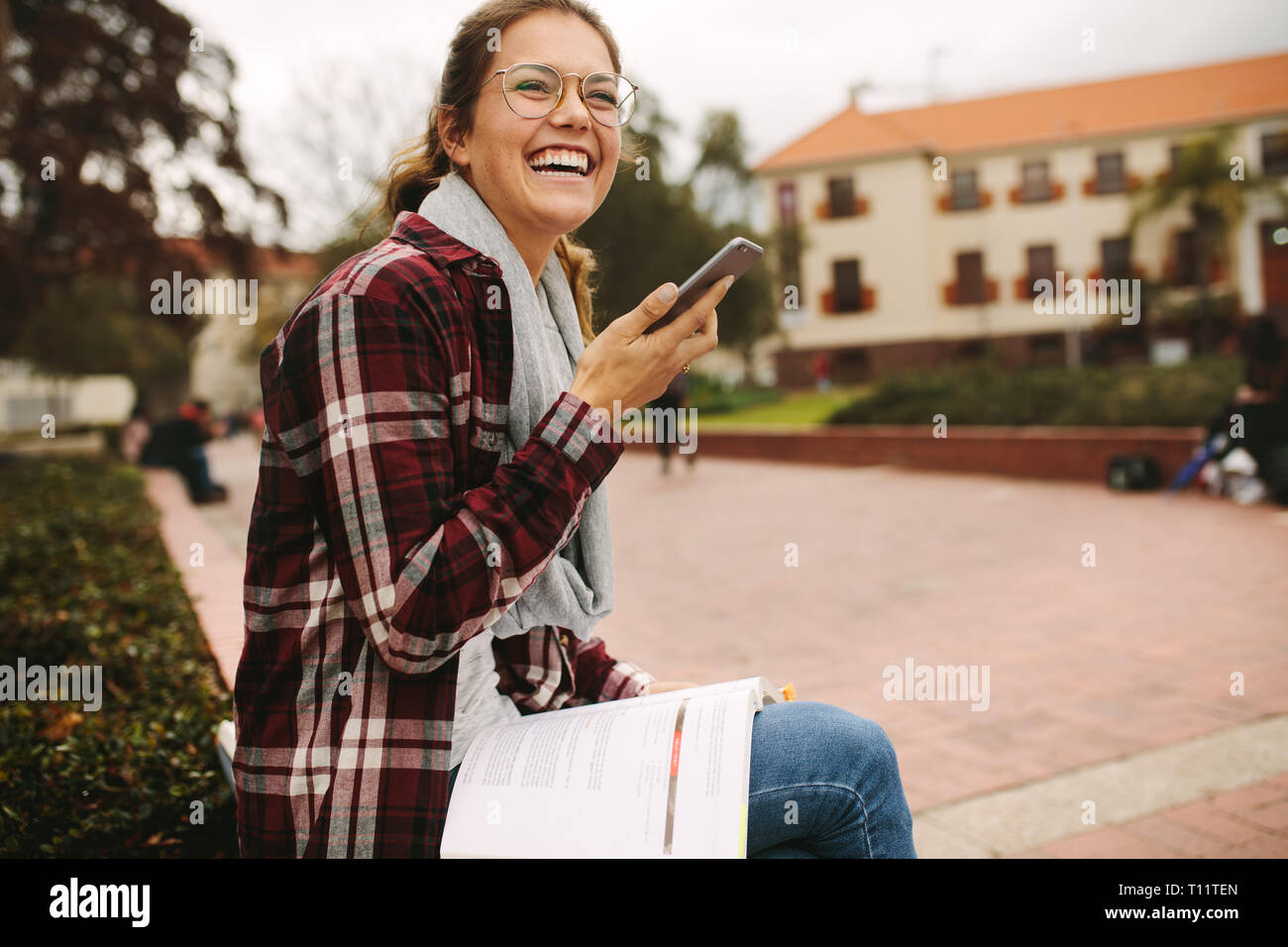 Smiling girl student sitting at university campus with book talking on ...