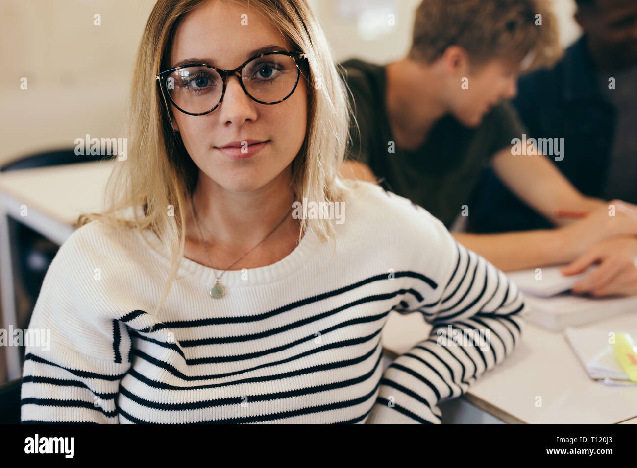 Young woman sitting at table with friends studying in background ...