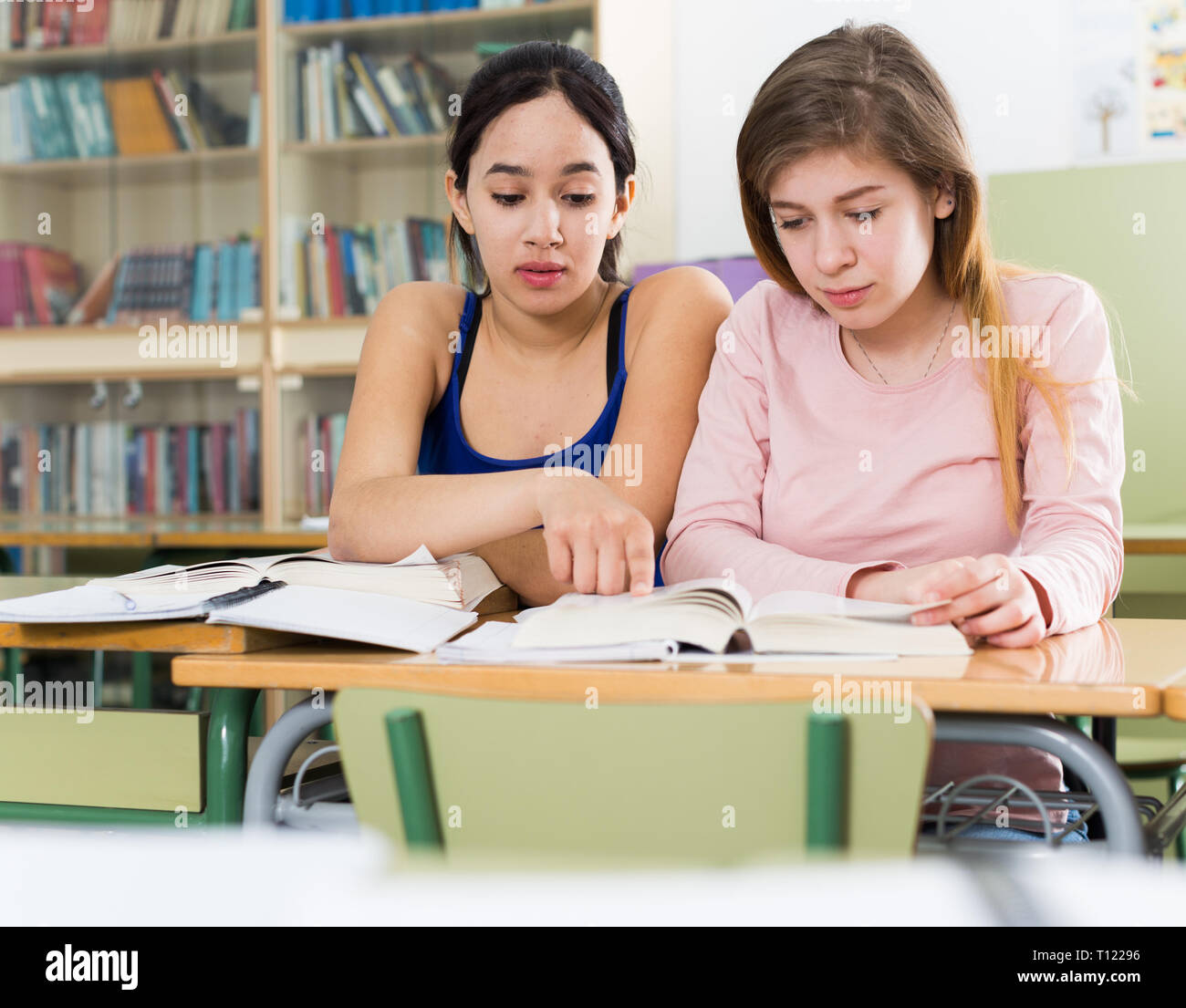Two girls are sitting at the desk and writing homework in the classroom ...
