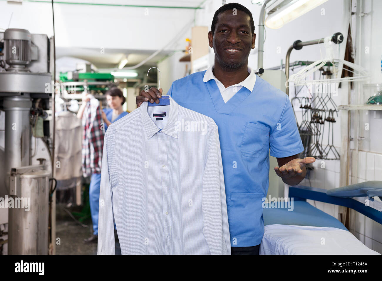 Smiling African-American man worker of laundry holding clean garments ...