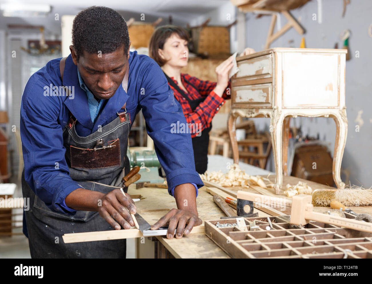 Woman and man carpenters using tools for restoration wooden bureau in ...