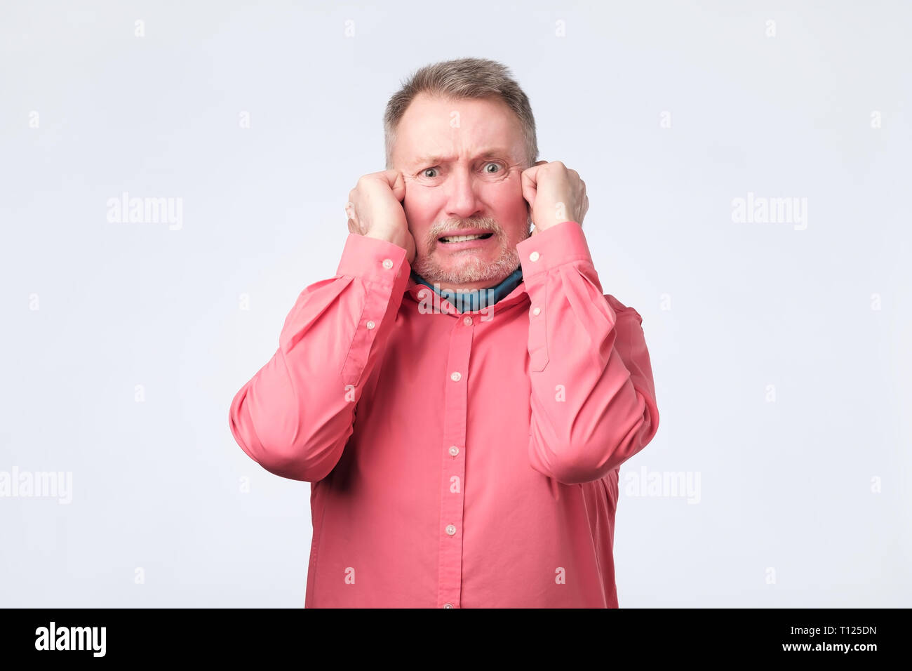 Senior man plugging ears with fingers . Studio shoot. Negative facial ...