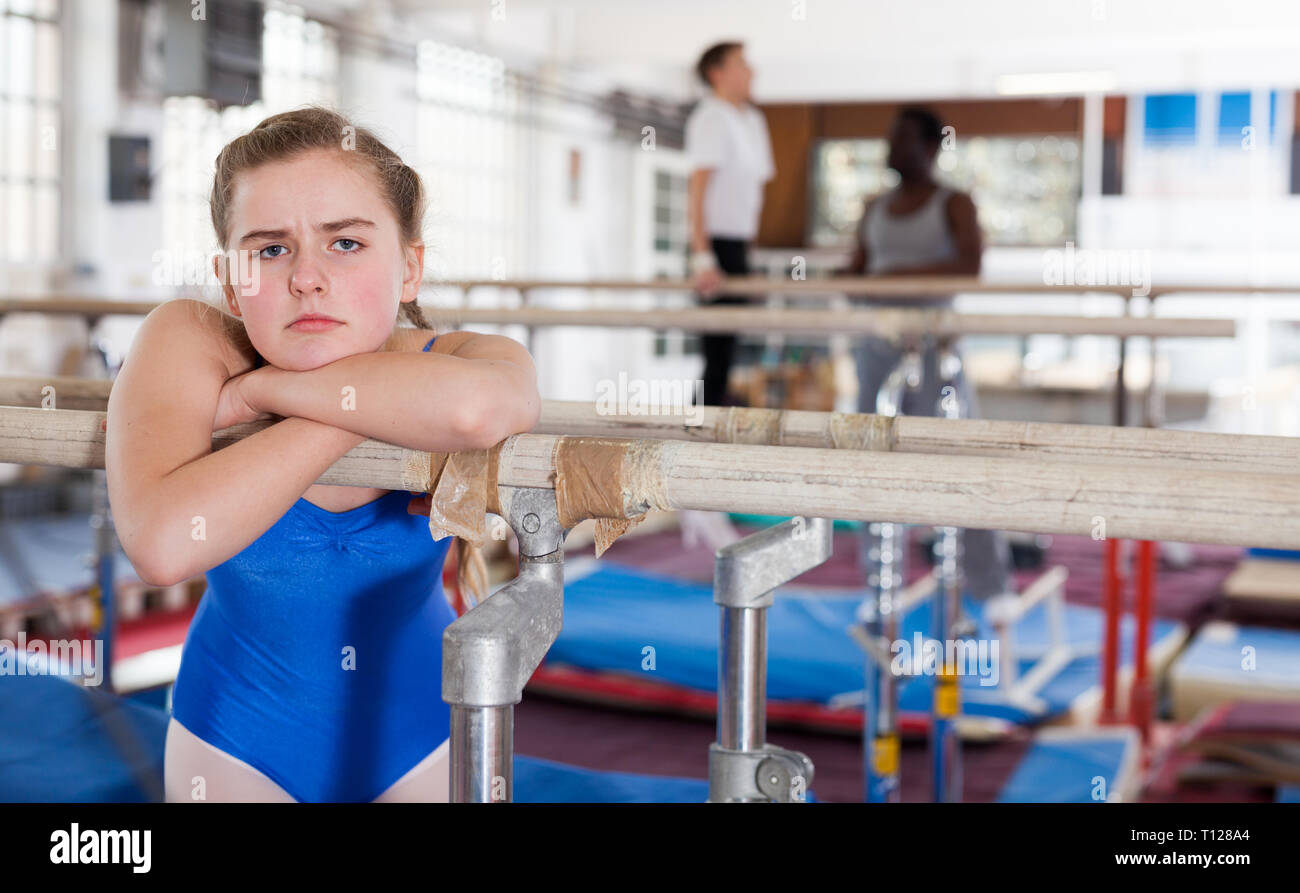 Portrait of sad teenage girl in gymnastic swimsuit posing near sports ...