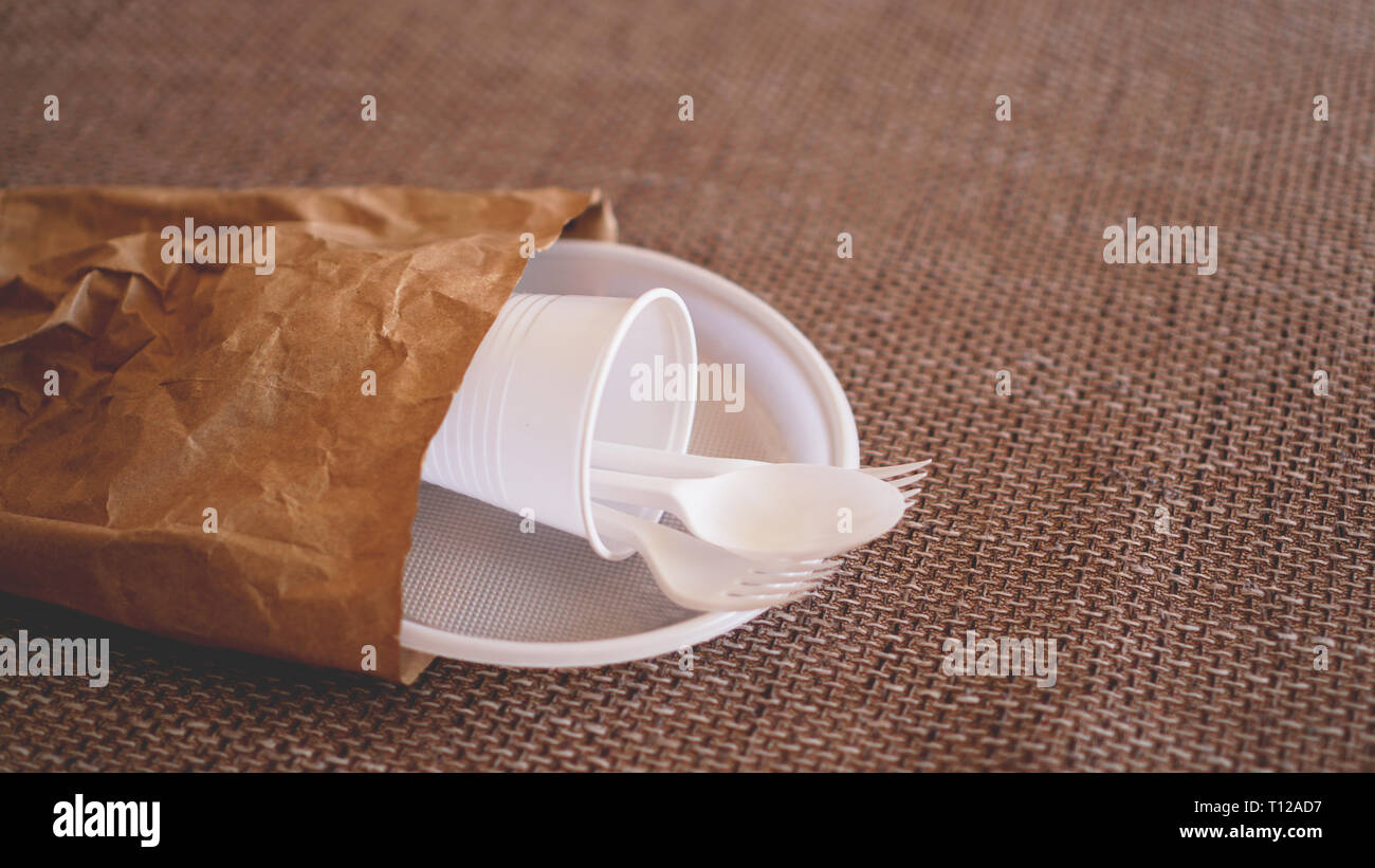 White plastic dishes in a paper packet on beige background. Concept of ...